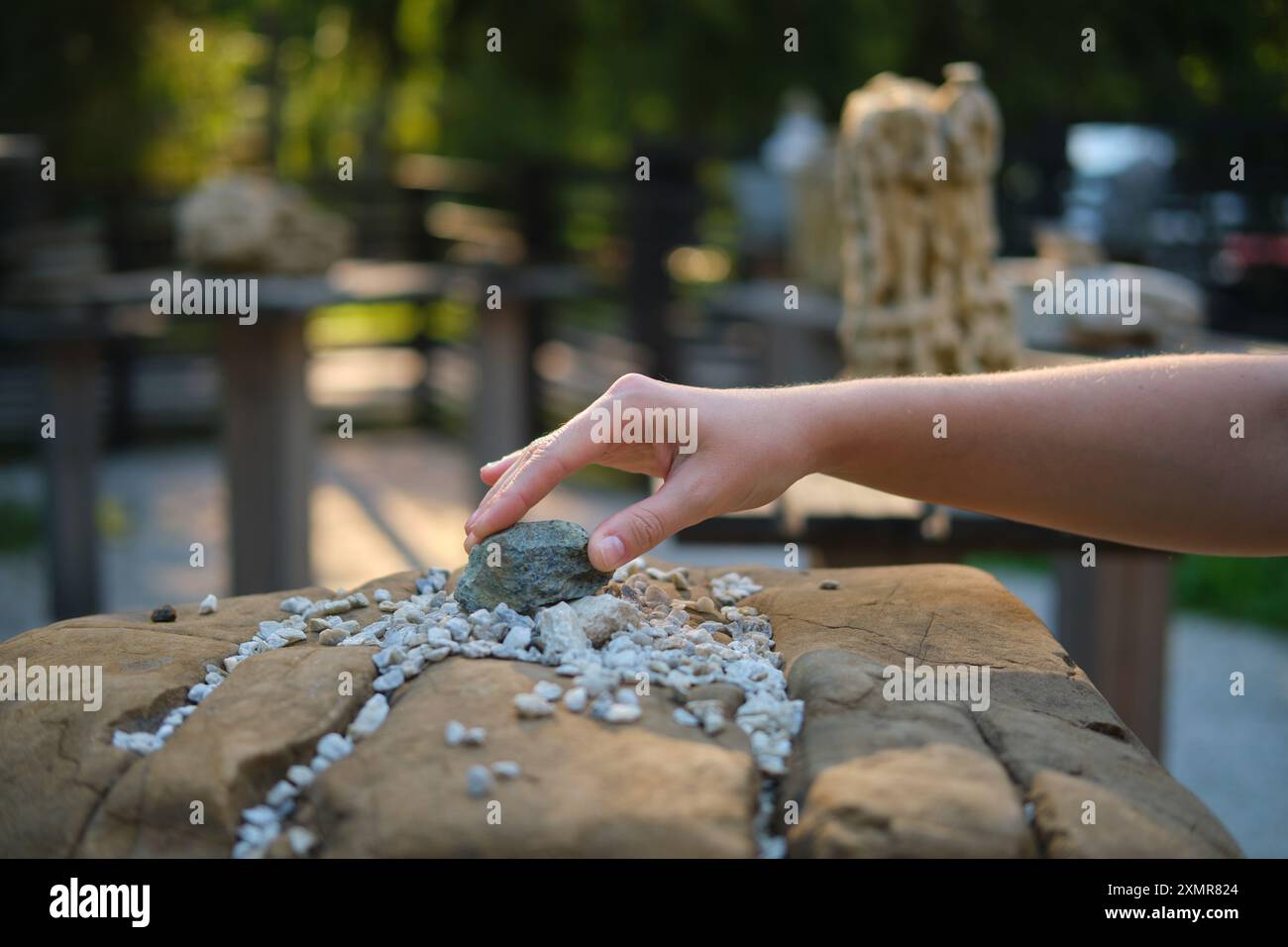 Hand placing a stone on a rock surface with small pebbles in an outdoor ...