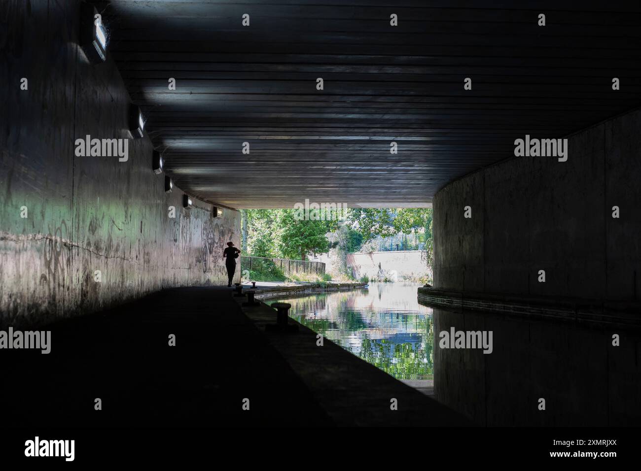 View of a lone female (in silhouette) walking by the side of a UK canal ...