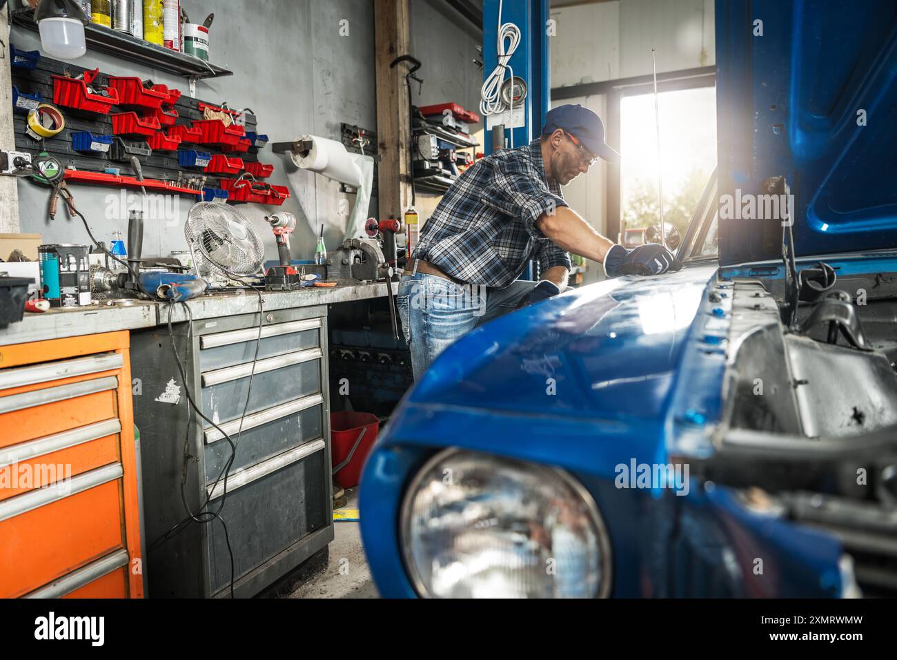 A skilled mechanic is focused on repairing a classic blue car in a well ...