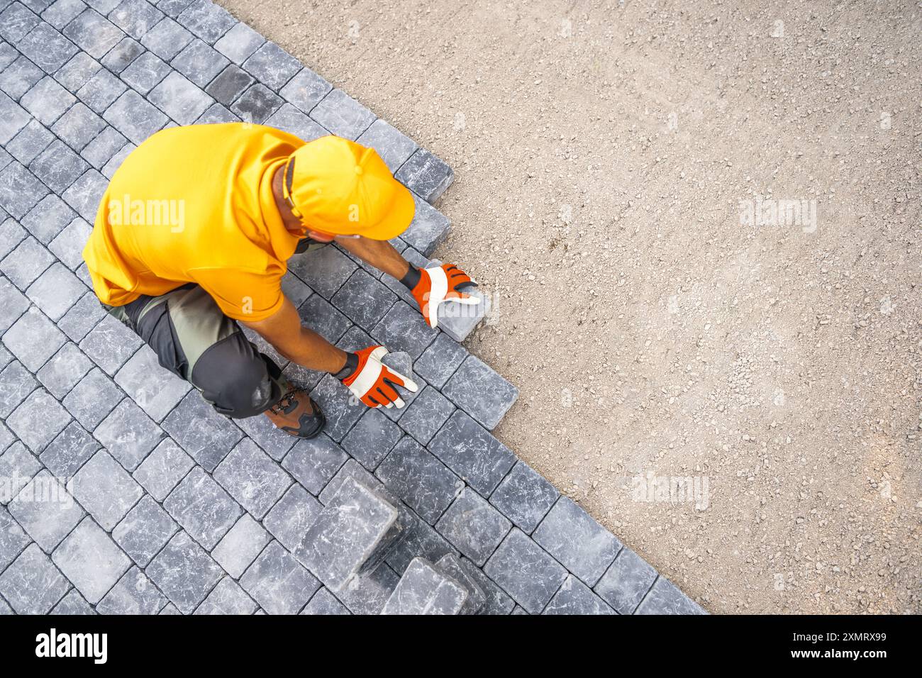 A construction worker is carefully placing gray paving stones onto a ...