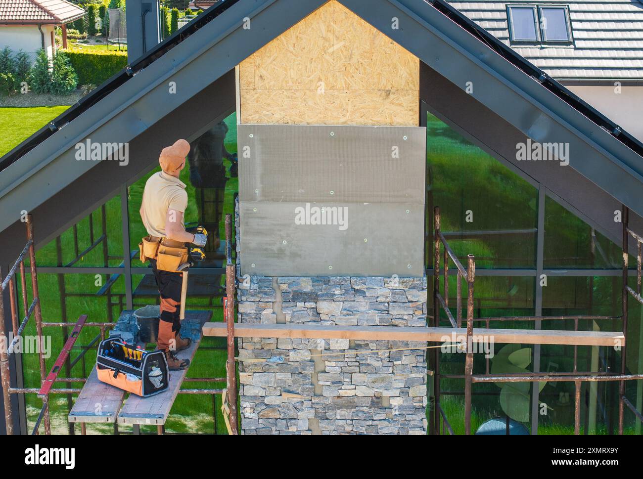 A construction worker is positioned on scaffolding, applying a stone ...