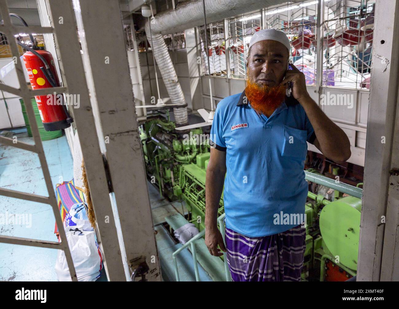 Bangladeshi man with red beard calling on phone in ferry engine room ...