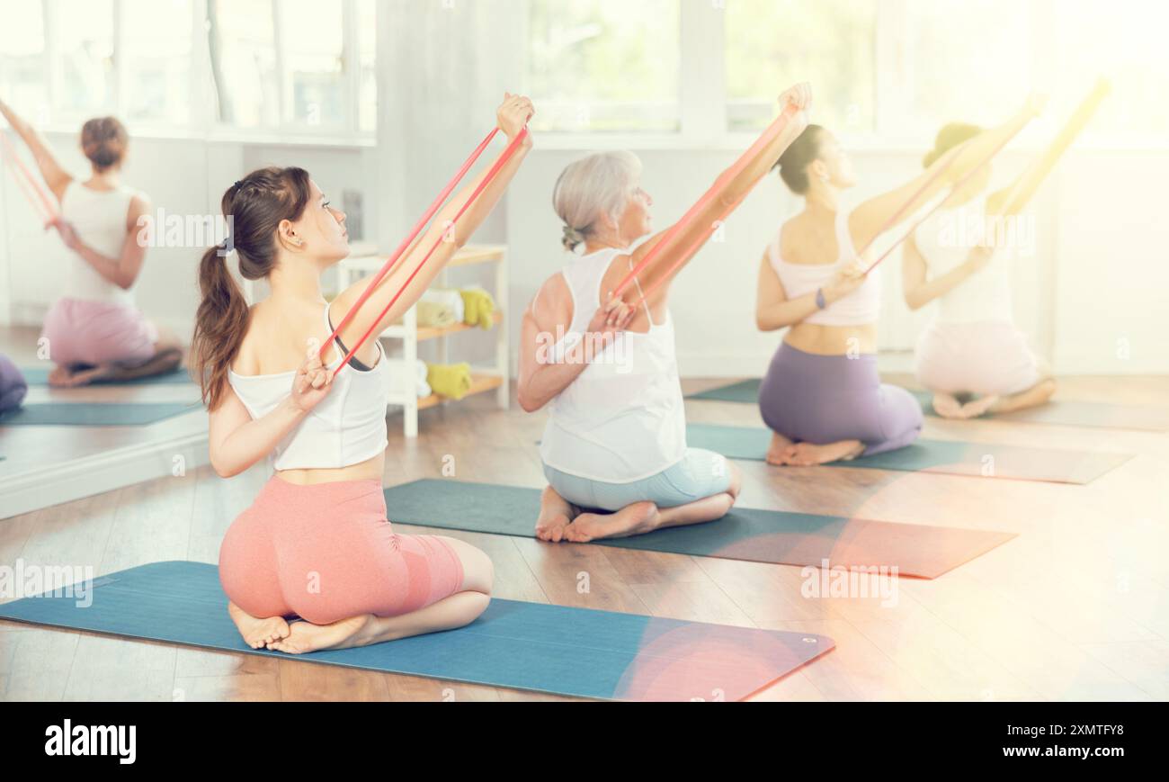 Women of different ages sit on mats and do pilates exercises with an ...