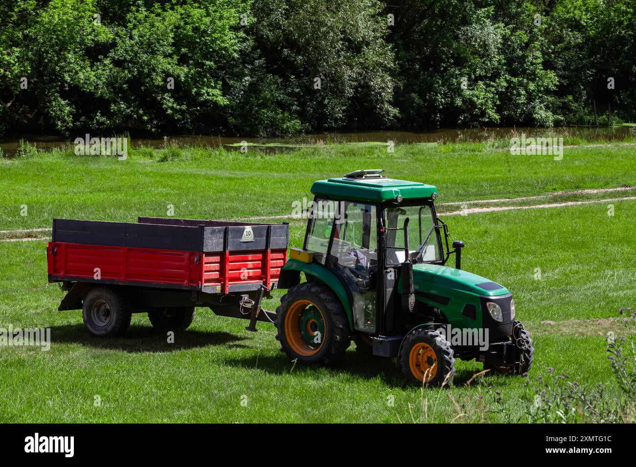 Compact tractor on a rural lawn with forest and river in the background ...