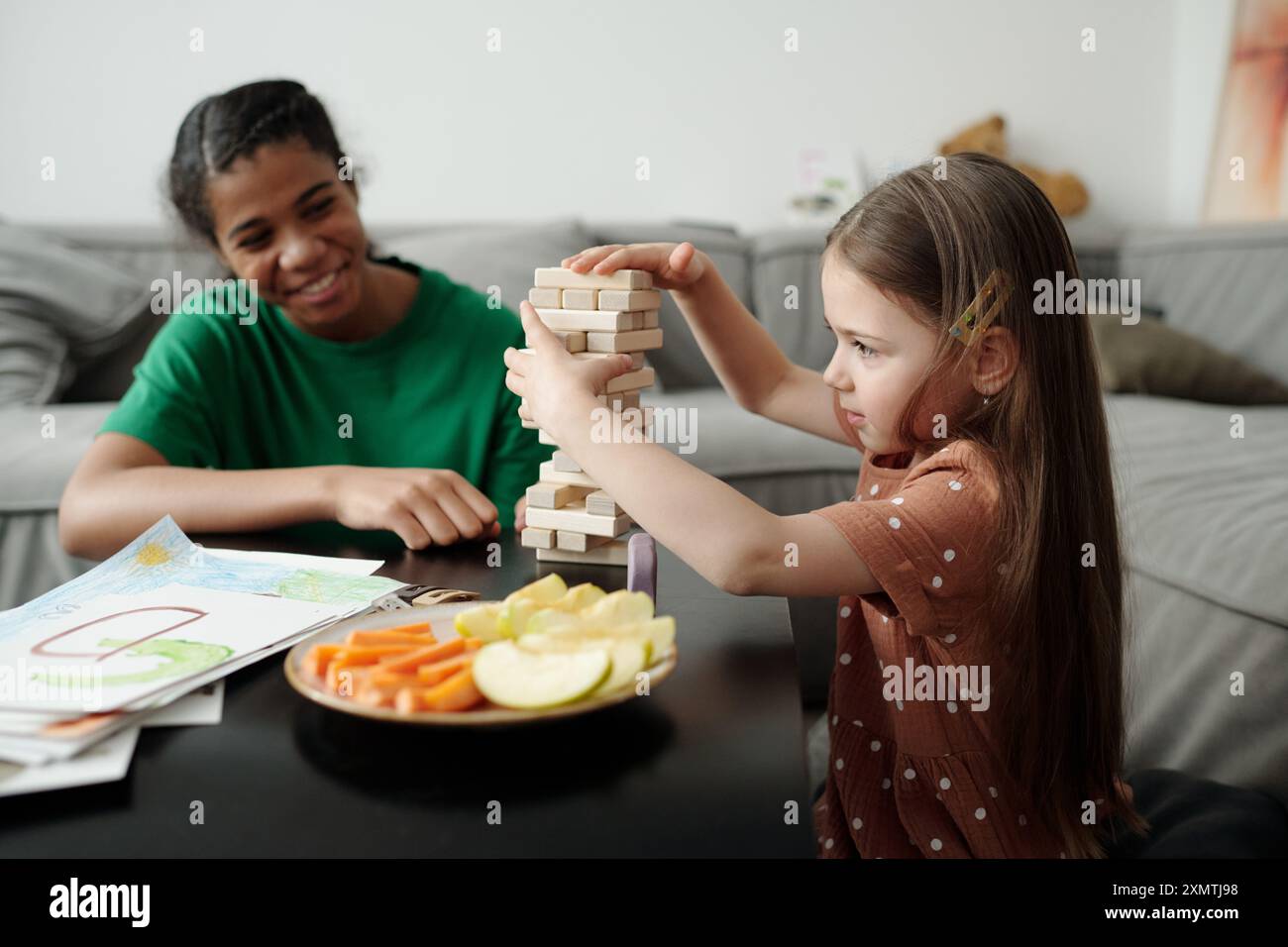 Adorable little girl building tower while putting wooden blocks on top ...