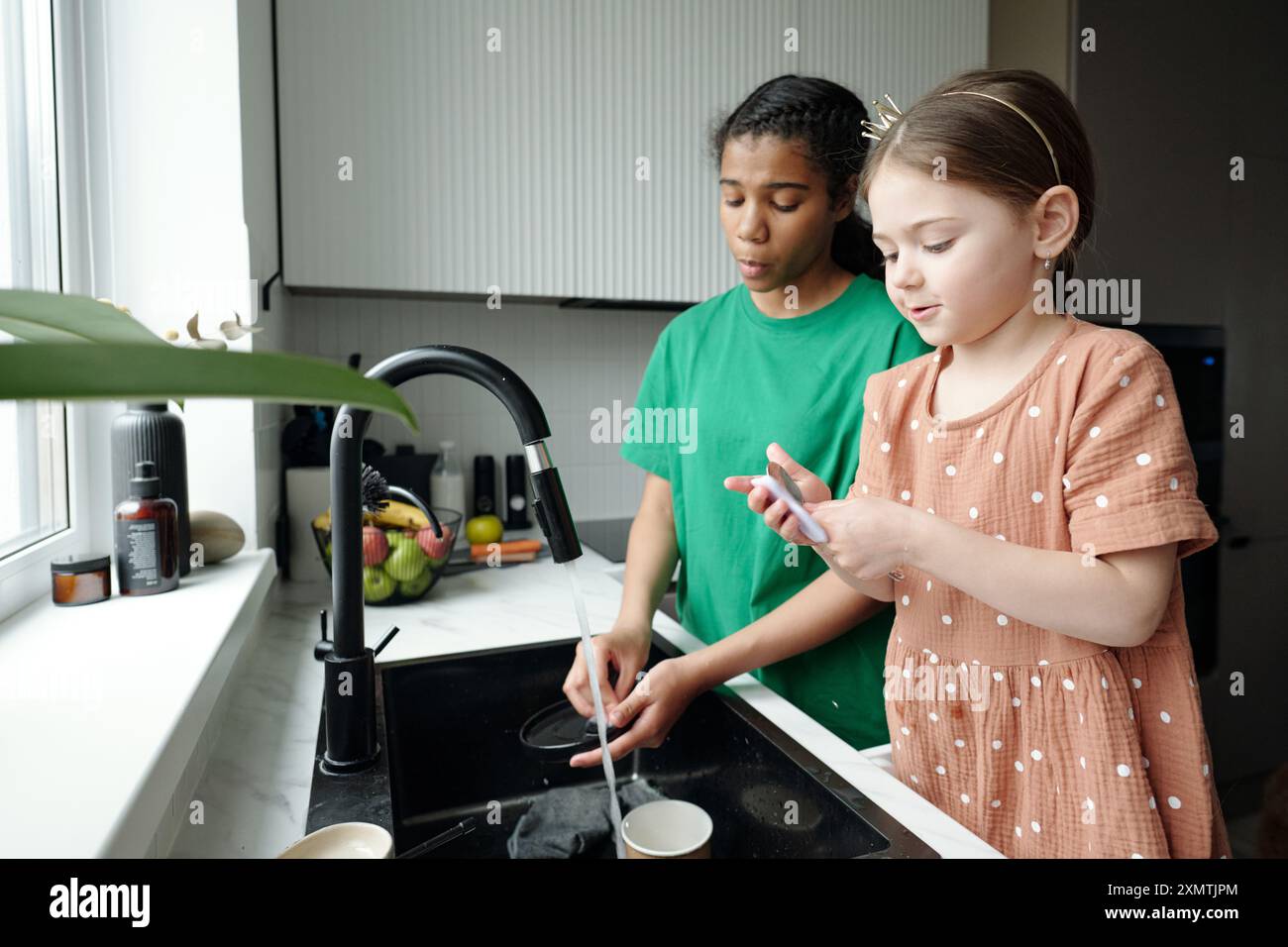 Adorable little girl wiping clean dishes with dry napkin while standing ...