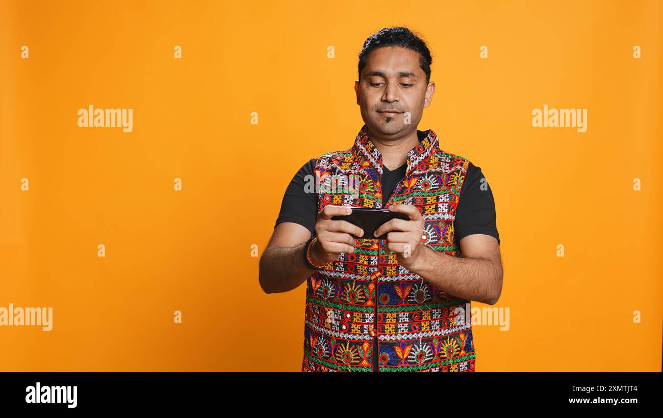 Indian man playing videogames on cellphone in landscape mode, enjoying ...