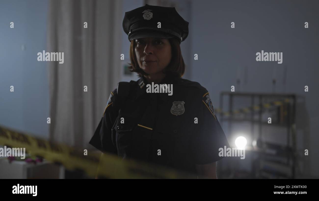 Hispanic woman police officer standing solemnly at a dimly lit indoor ...