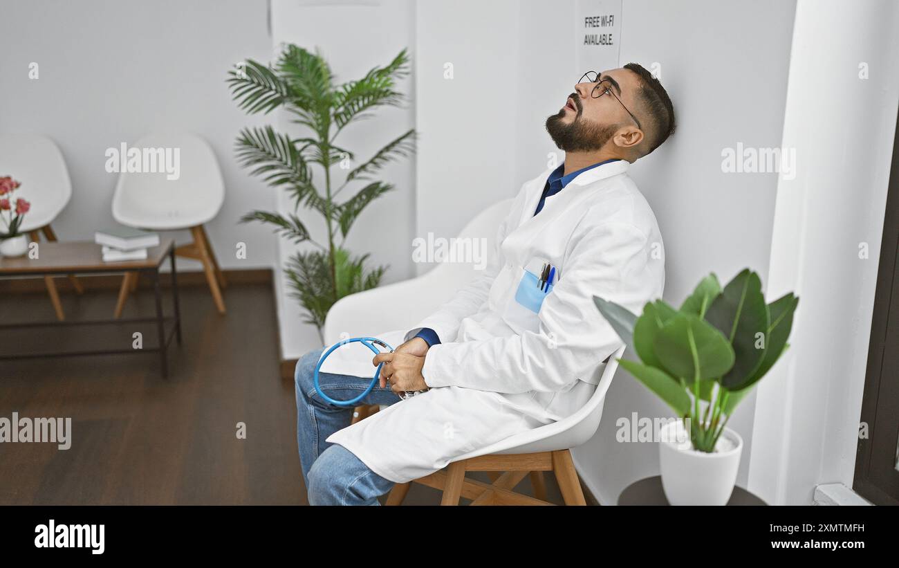 A tired young man with a beard wearing glasses and a lab coat resting ...