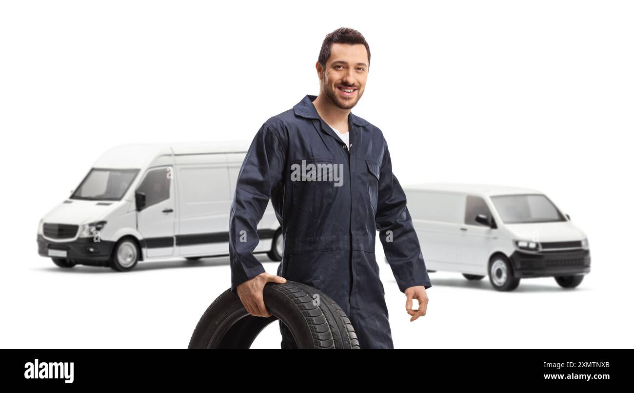 Auto mechanic smiling and holding a tire in front of vans isolated on ...