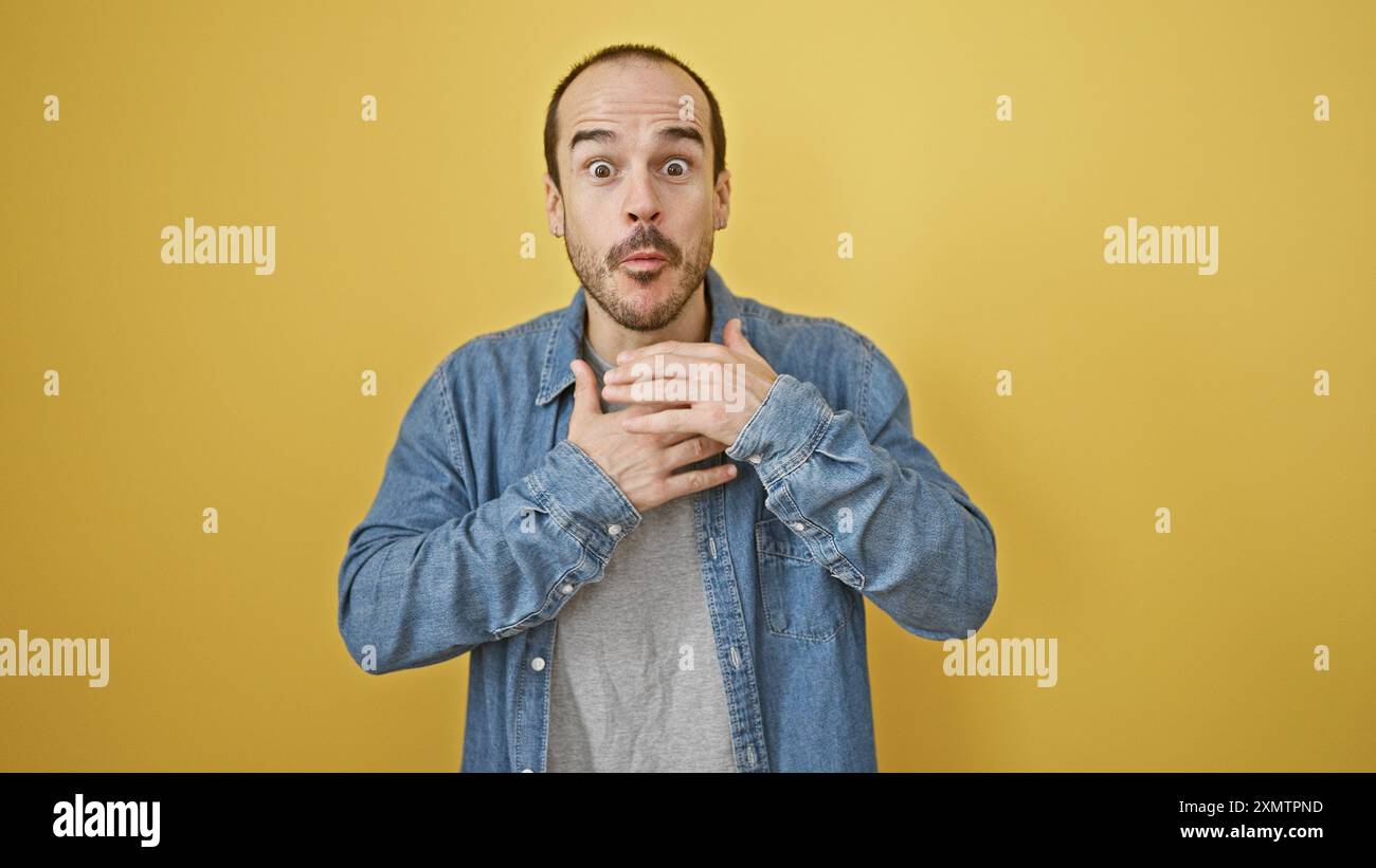 Bald hispanic man with beard in denim shirt over yellow background ...