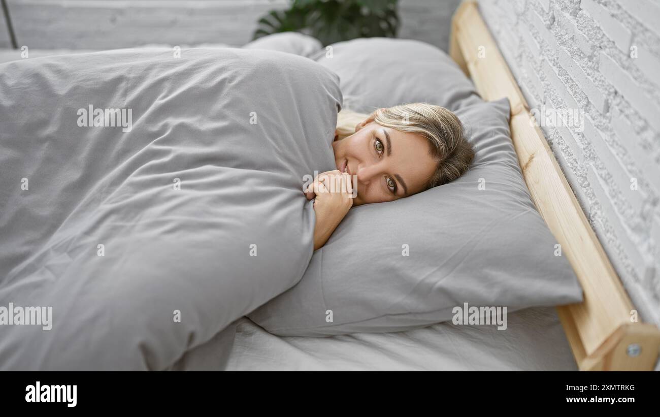 Beautiful blonde woman lying in bed with a serene expression, in a cozy ...
