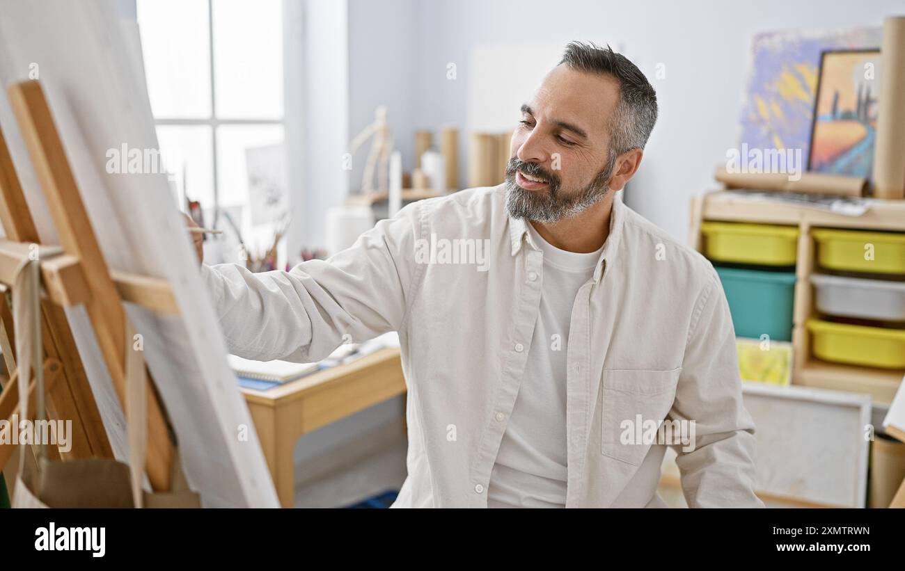 A mature latin man with grey beard smiles while painting in a well-lit ...
