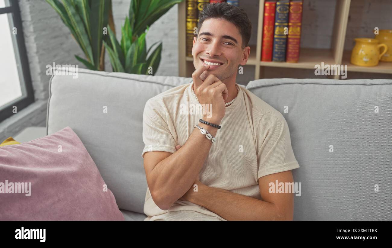 Handsome hispanic man smiling casually while sitting on a grey sofa in ...