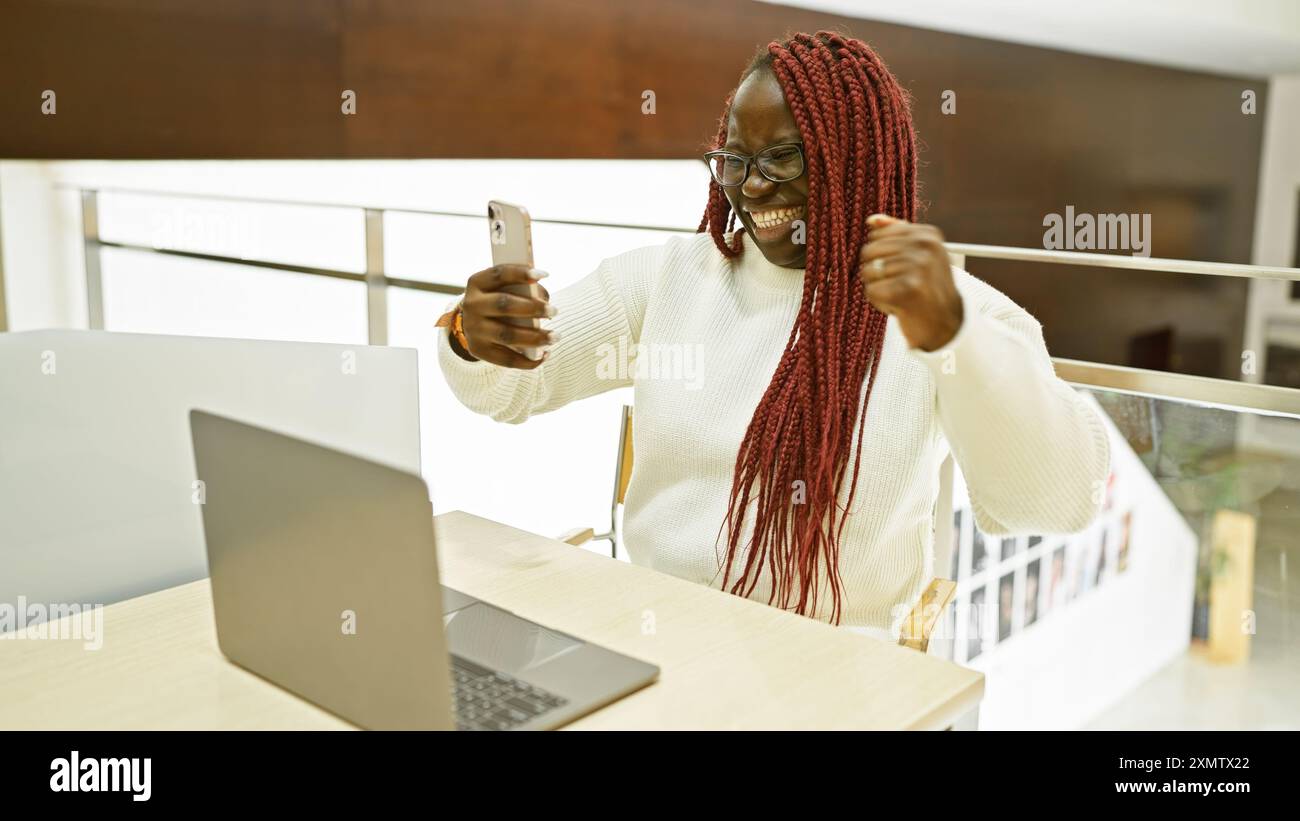 Smiling african american woman with braids using smartphone in a modern ...