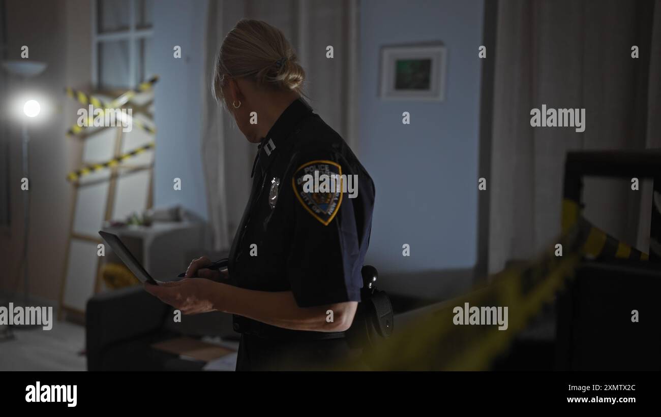 A blonde woman police officer examines a tablet at a taped-off indoor ...