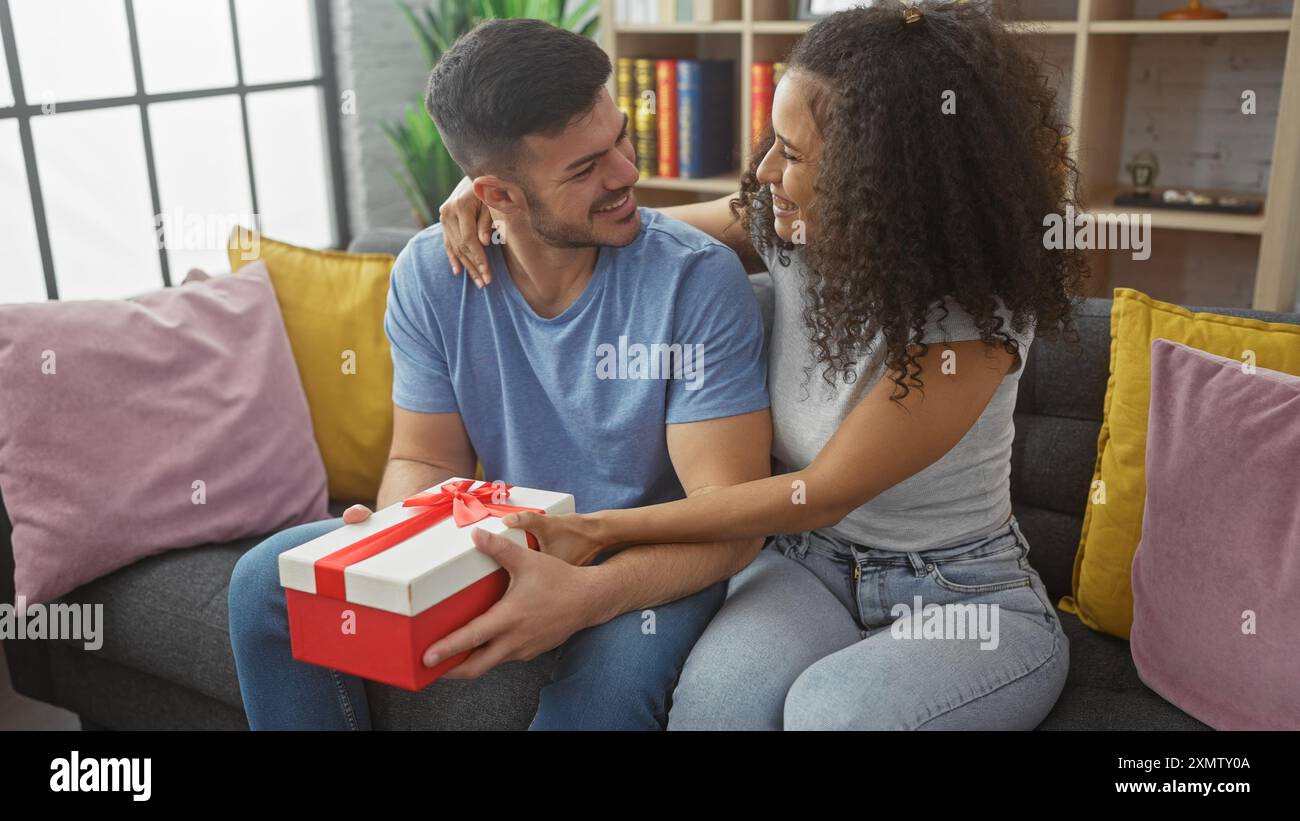 A man and woman lovingly exchange a gift on a cozy sofa in a modern ...