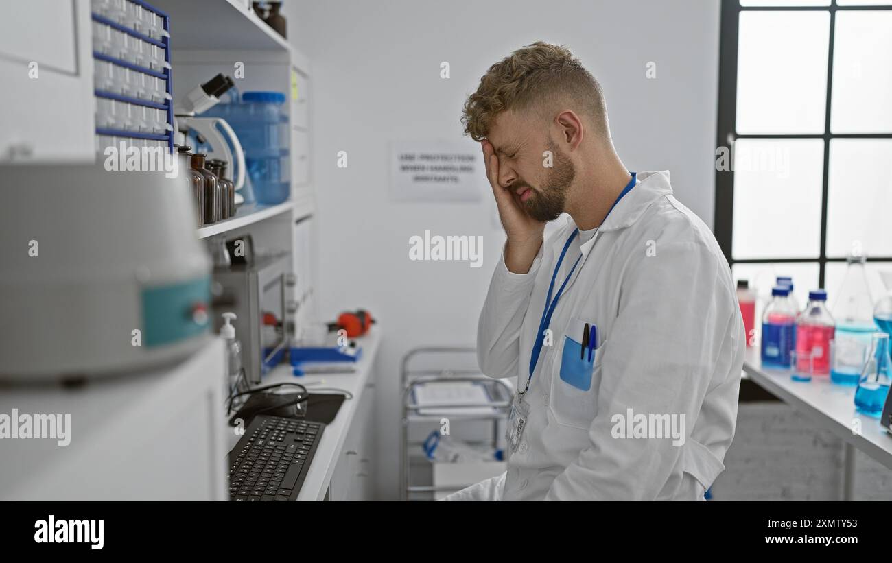 Stressed young man in lab coat standing in a laboratory with his hand ...