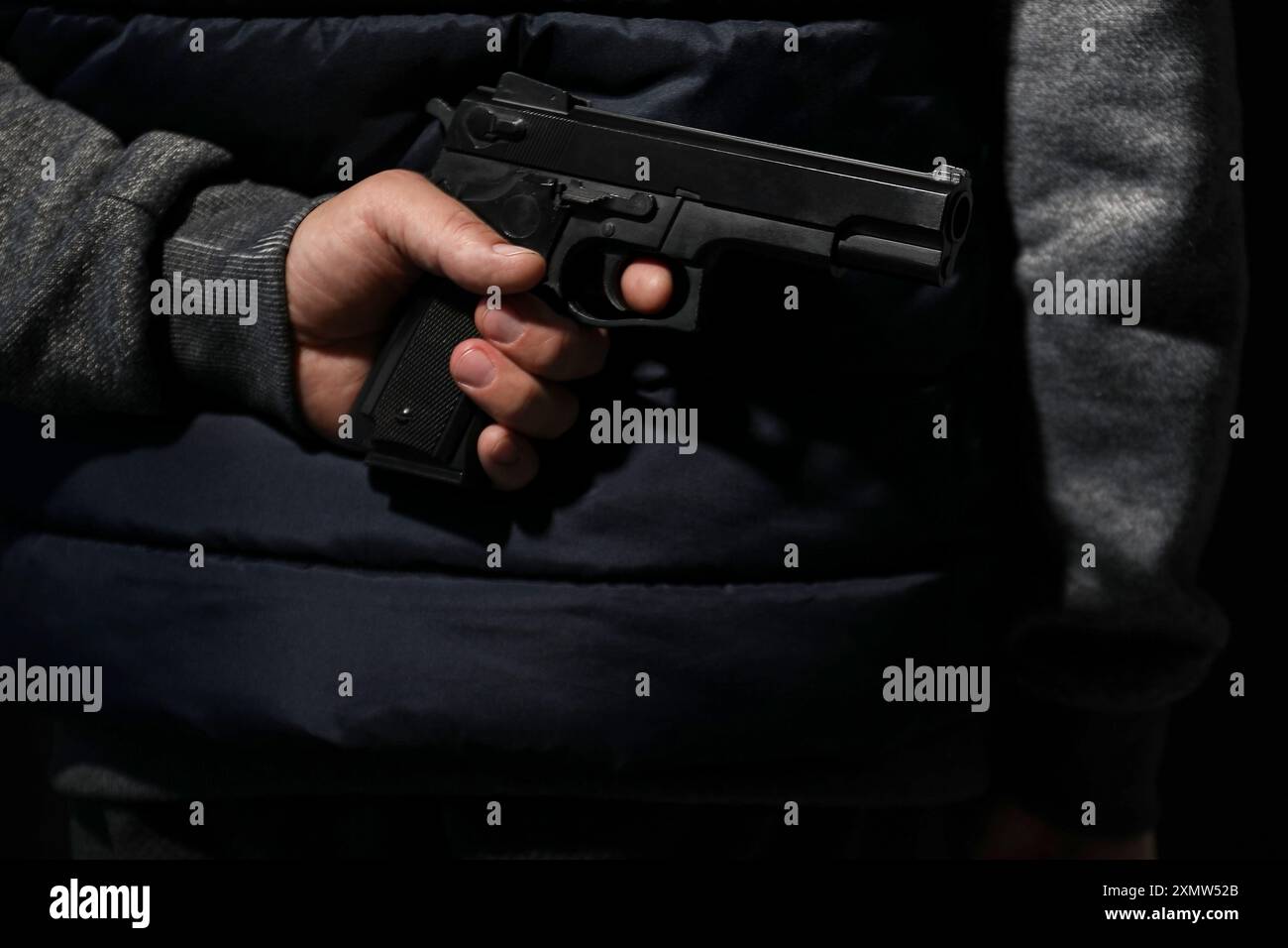 Man hiding gun behind his back on black background, closeup. Armed ...
