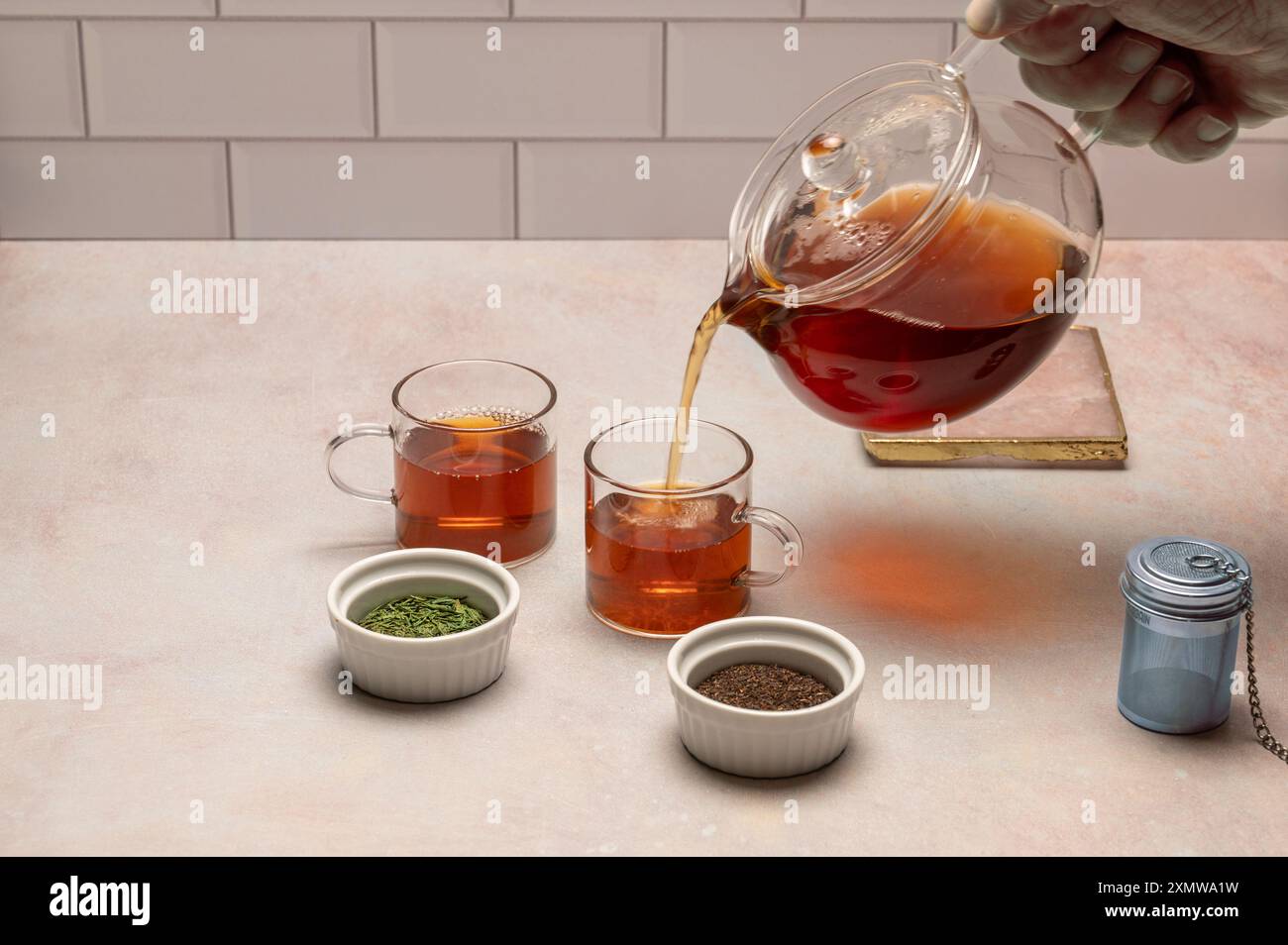 Hand pouring tea from tea pot into glass cups, with brewing sieve and ...