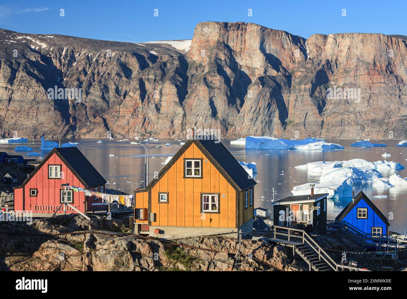 Typical greenlandic houses in front of icebergs and mountains, sunny ...