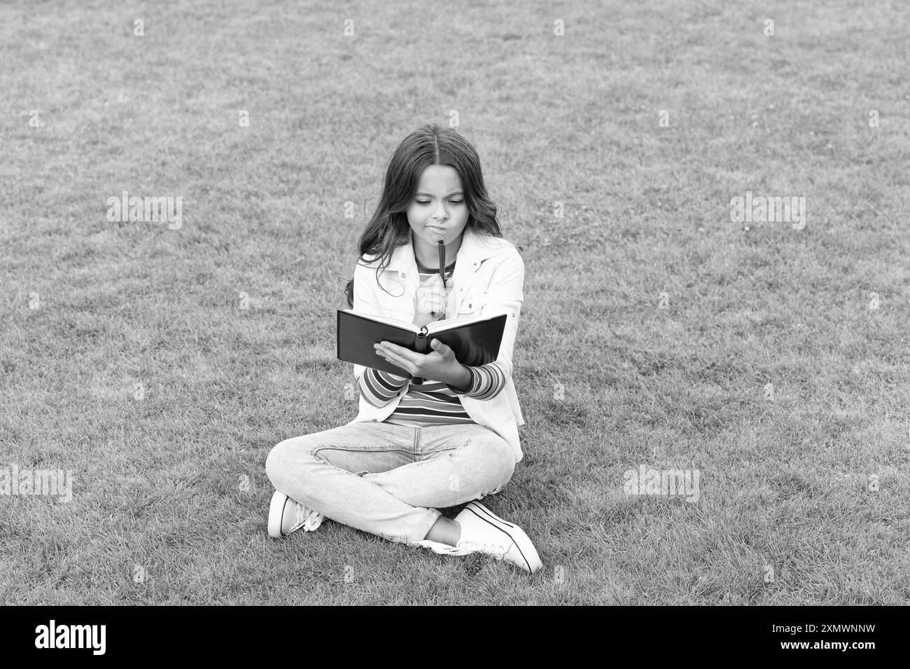 thinking teen child making notes in notebook sitting on grass. taking ...
