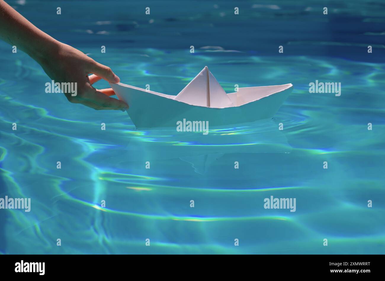 Paper boat sailing on water causing waves and ripples. Hand putting a ...