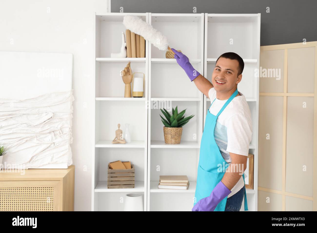Male janitor cleaning shelf with pp-duster in room Stock Photo - Alamy