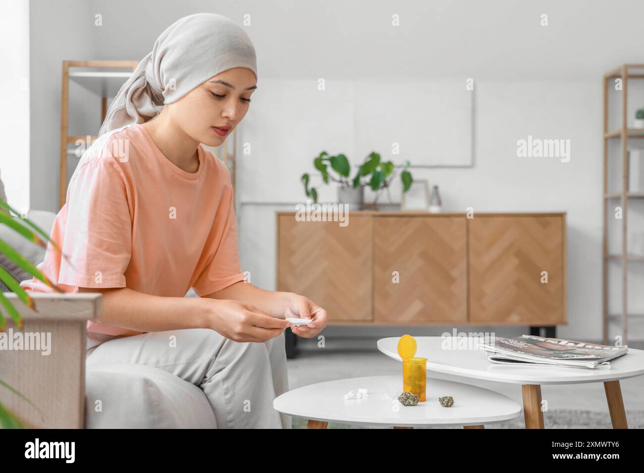 Young Asian woman after chemotherapy rolling joint with weed on sofa at ...