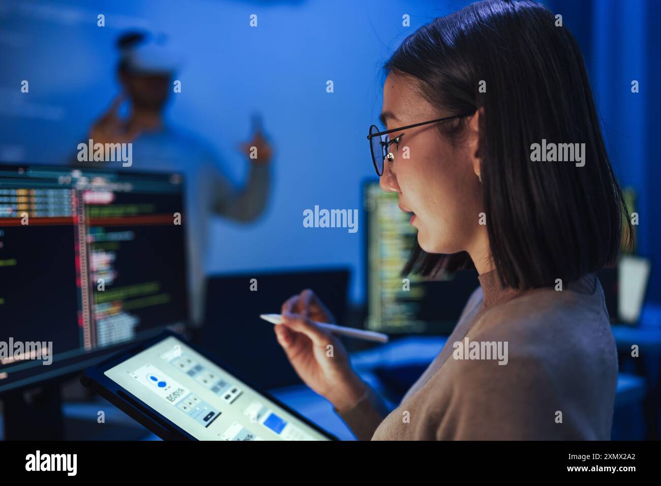 Asian UX designer works on a tablet while a colleague tests a VR ...