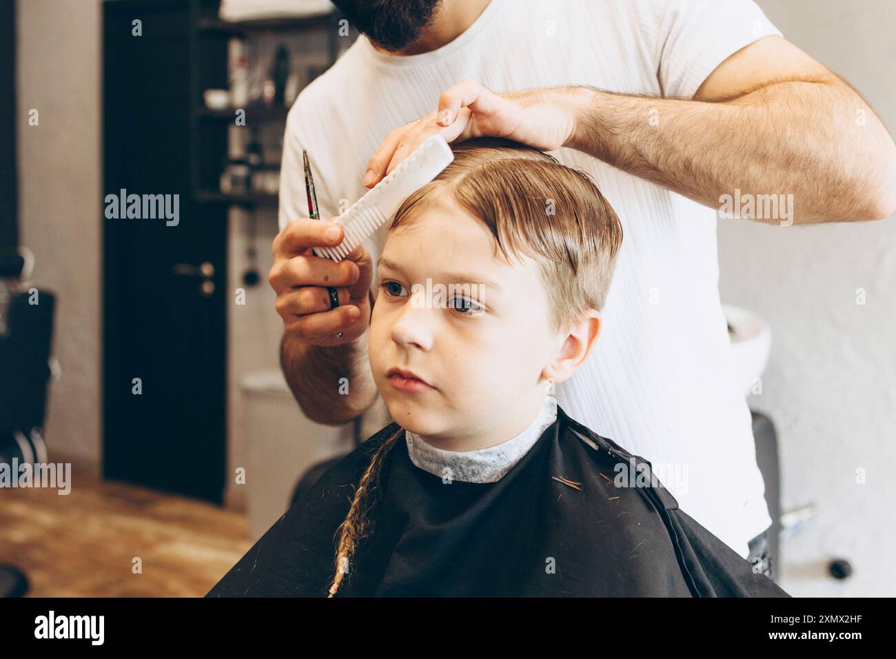 process of cutting a blond boy with a long braid in a chair in a ...