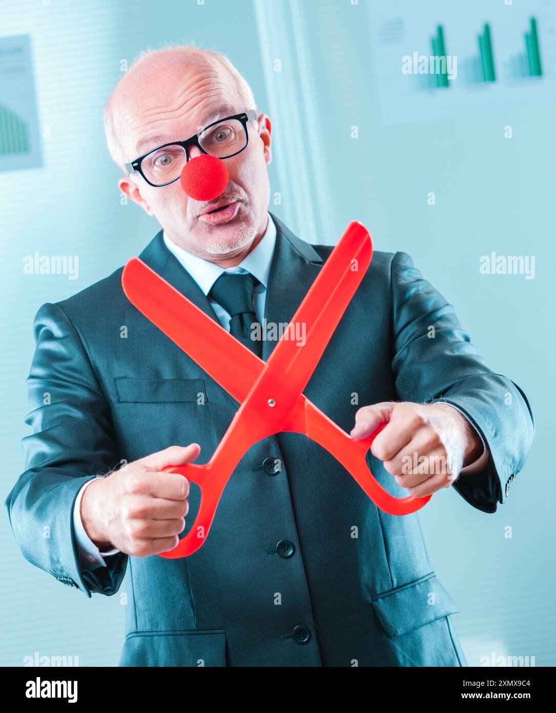 Old man in a suit wearing a clown nose and holding oversized red scissors, representing the ...