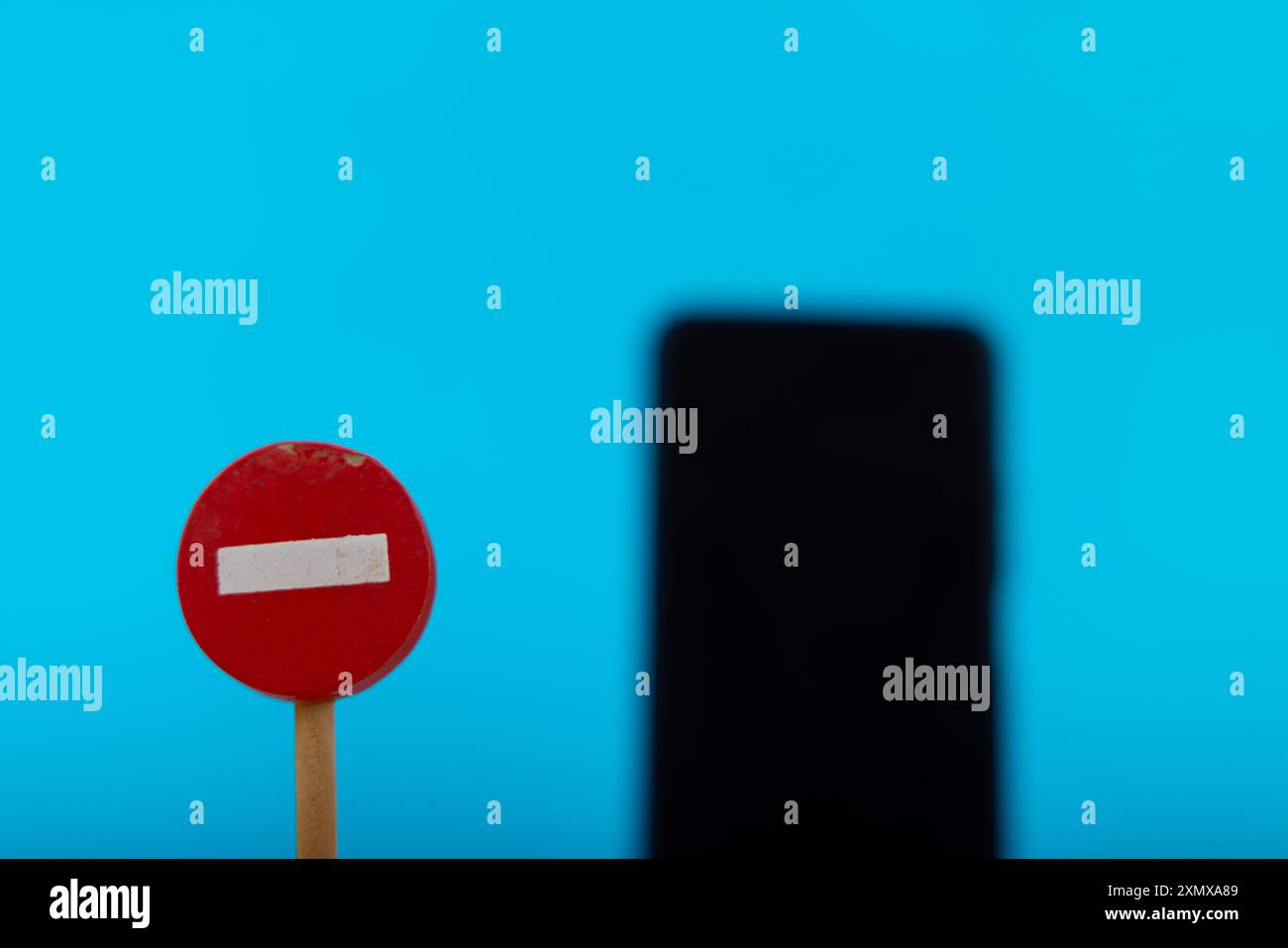 A wooden toy "No Entry" sign is paired with a smartphone on a blue ...