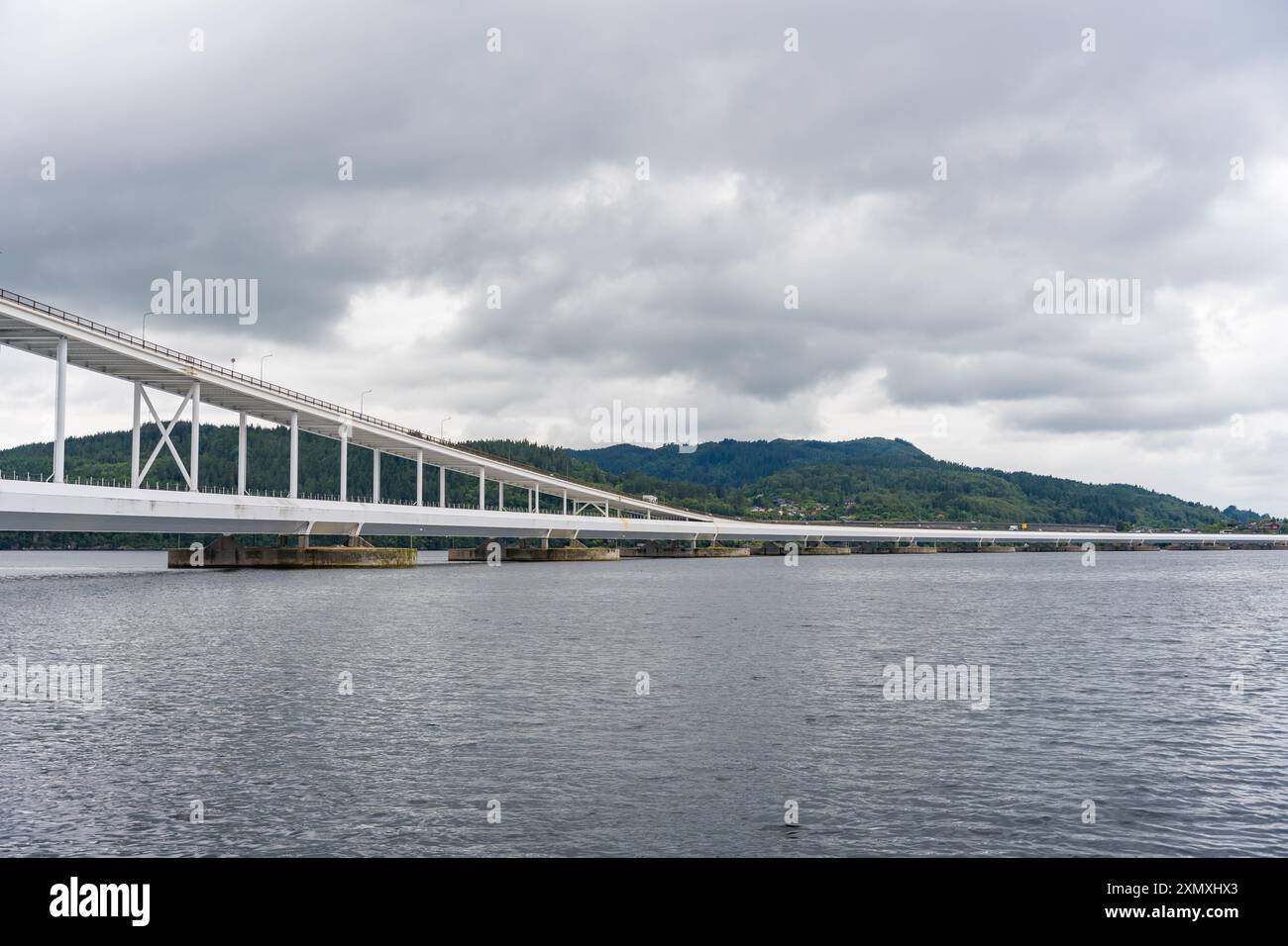 Long Osteroy bridge in Norway against green hills and grey sky, water ...