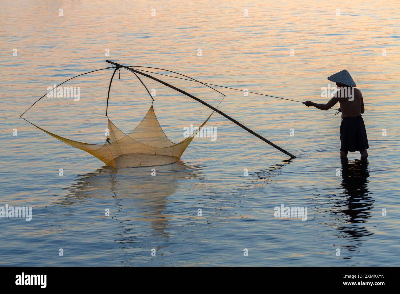 Vietnamese fisherman with traditional fishing net at sunrise on Quang ...