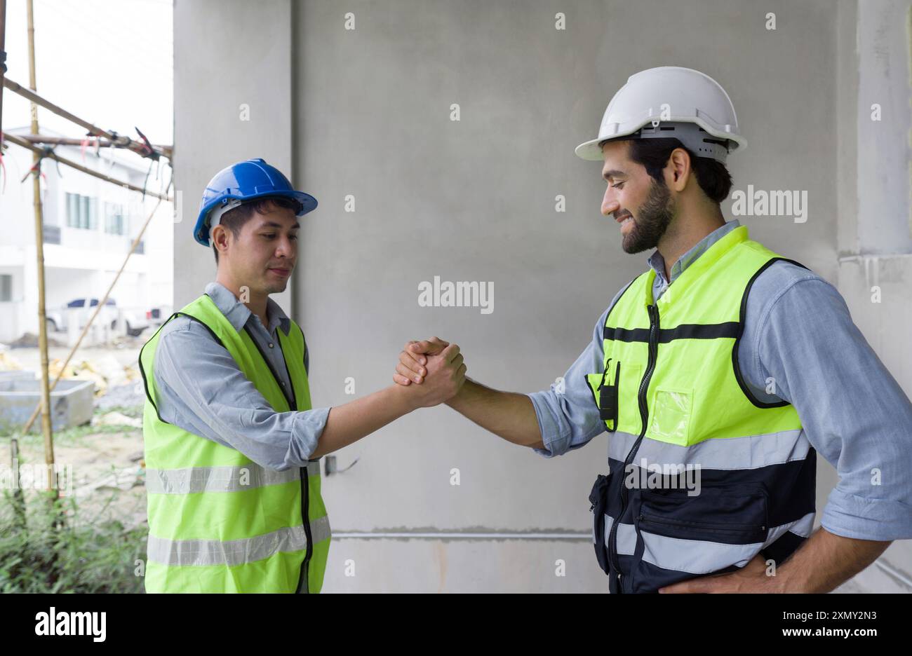 Two construction workers in safety vest and helmet join hands together ...