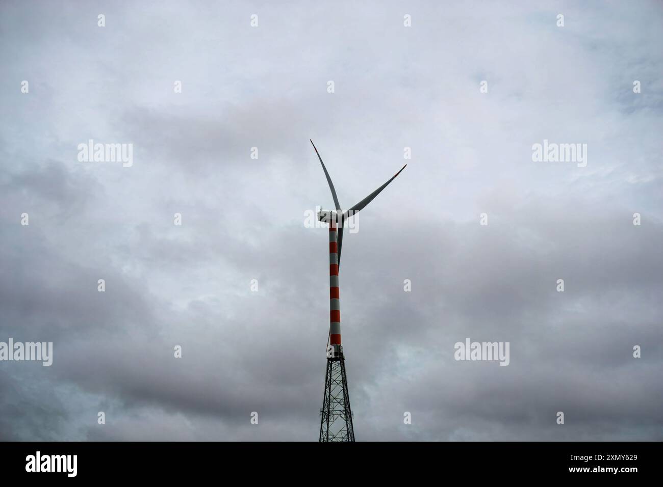 The wind turbine stands tall against the backdrop of a cloudy sky ...