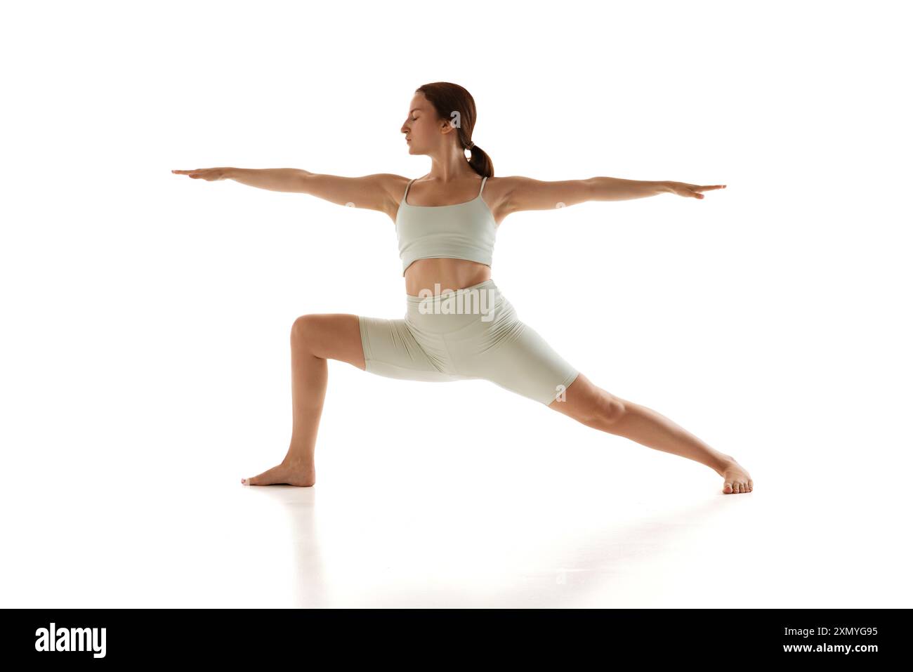 Woman in athletic wear performs yoga pose, with one knee bent and arms ...