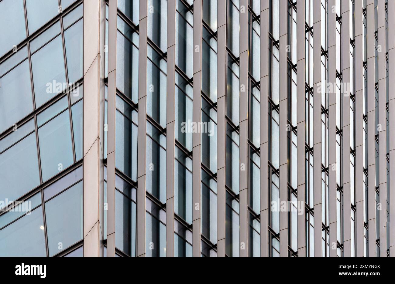 The sleek facade of a modern glass building reflects overcast skies ...