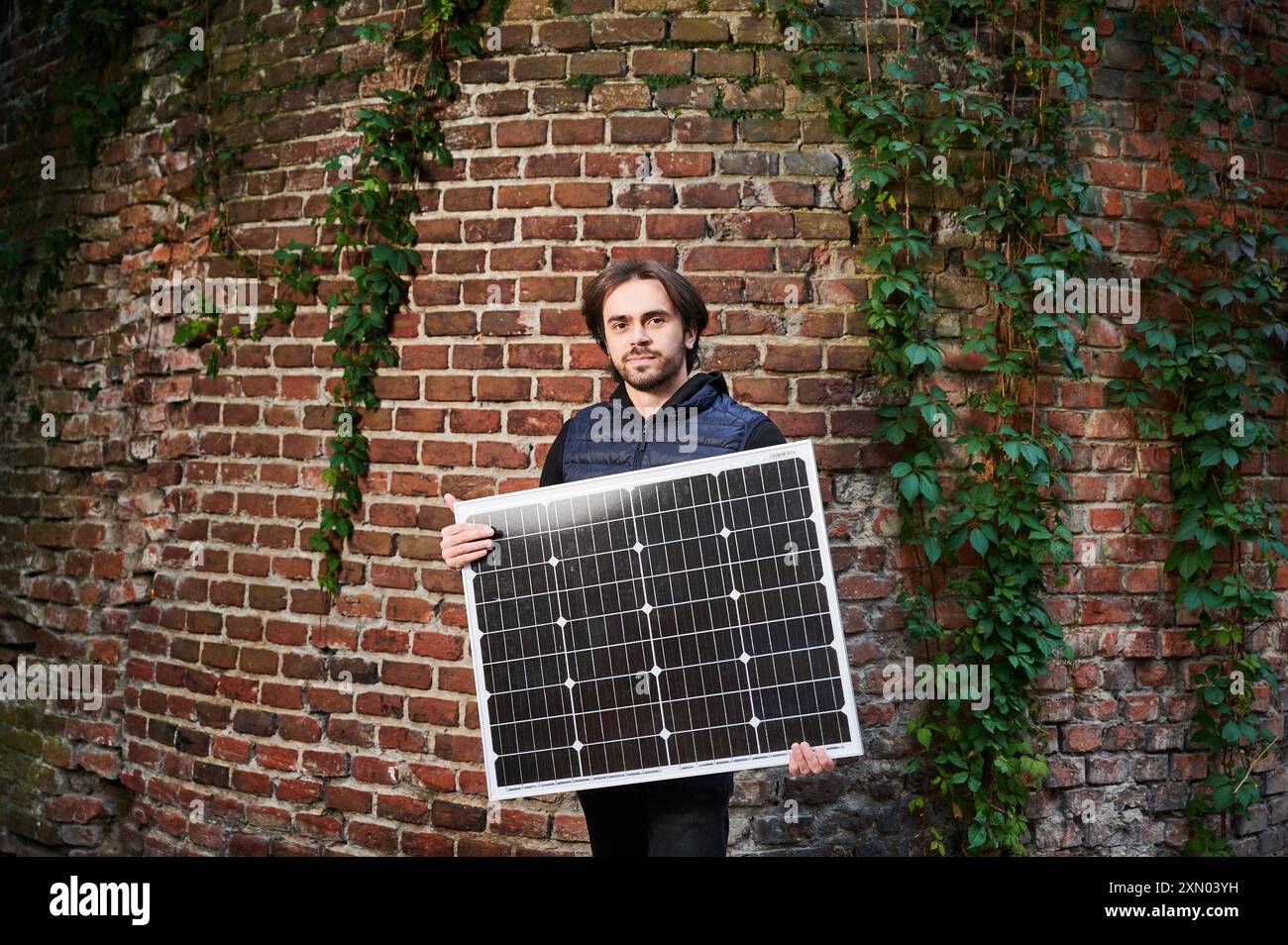 Portrait of man holding solar panel in front of old brick wall covered ...