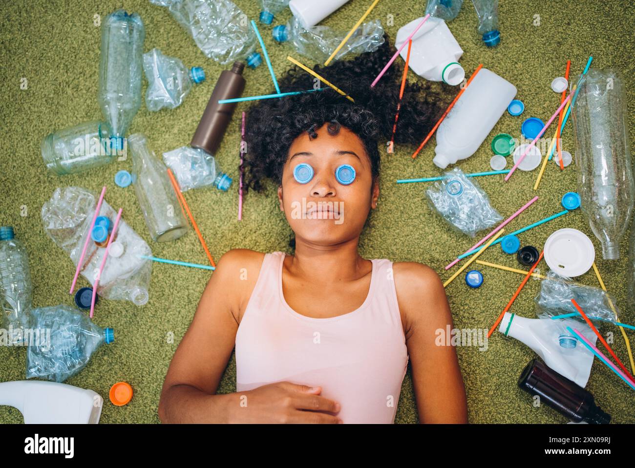 Young woman lying on carpet grass surrounded by plastic bottles and ...