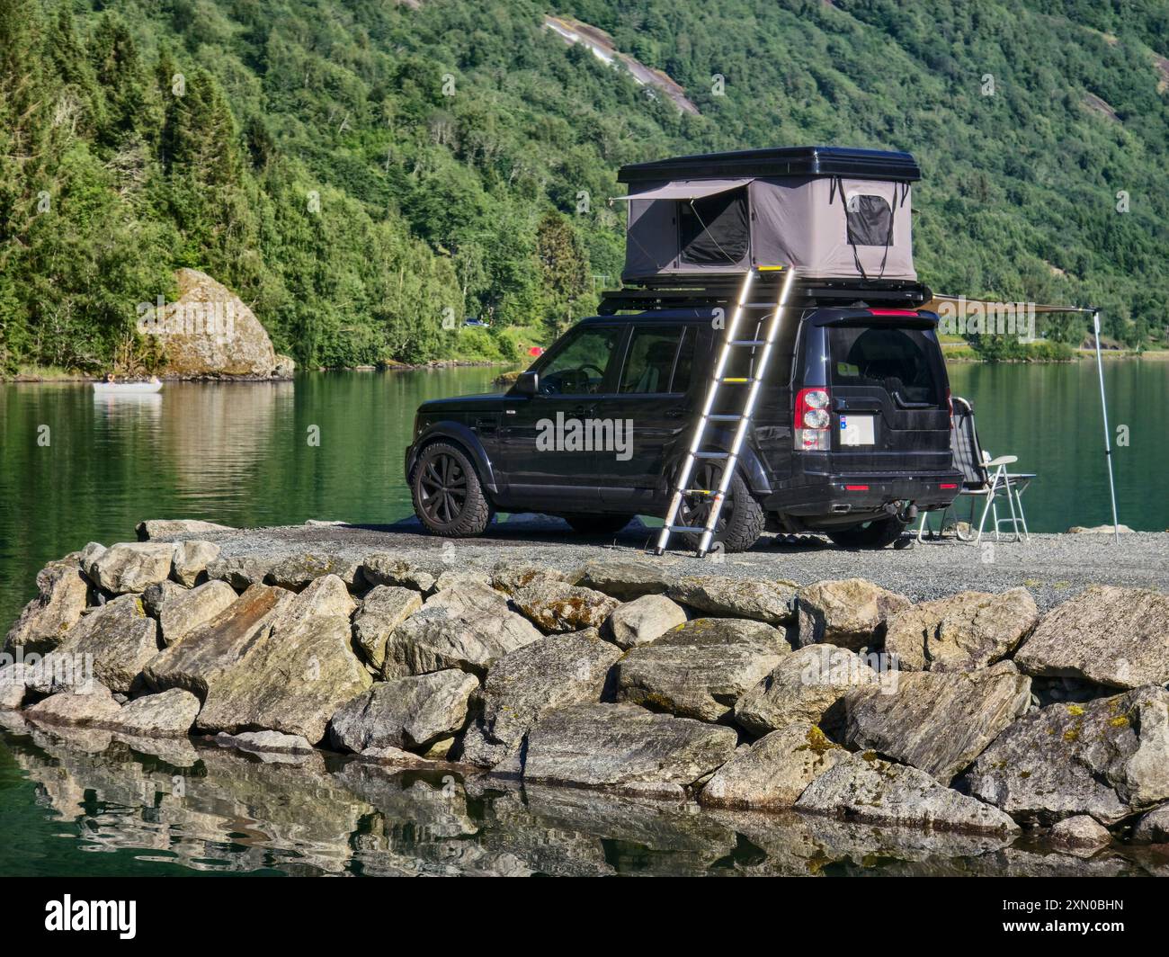 A rugged vehicle with a rooftop tent is parked by a tranquil lake ...