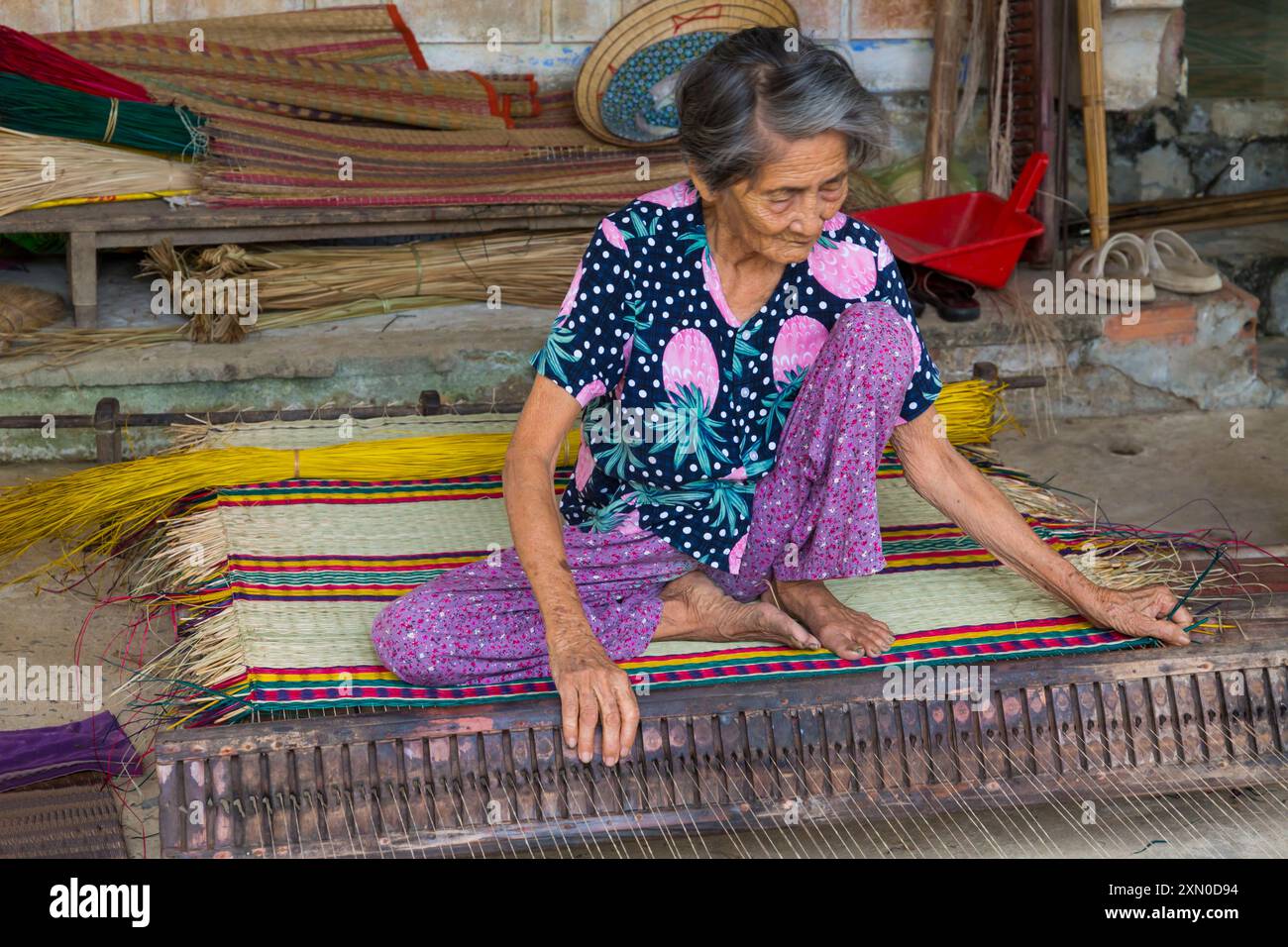 Elderly Vietnamese woman weaving sleeping mats from dried & dyed reeds ...
