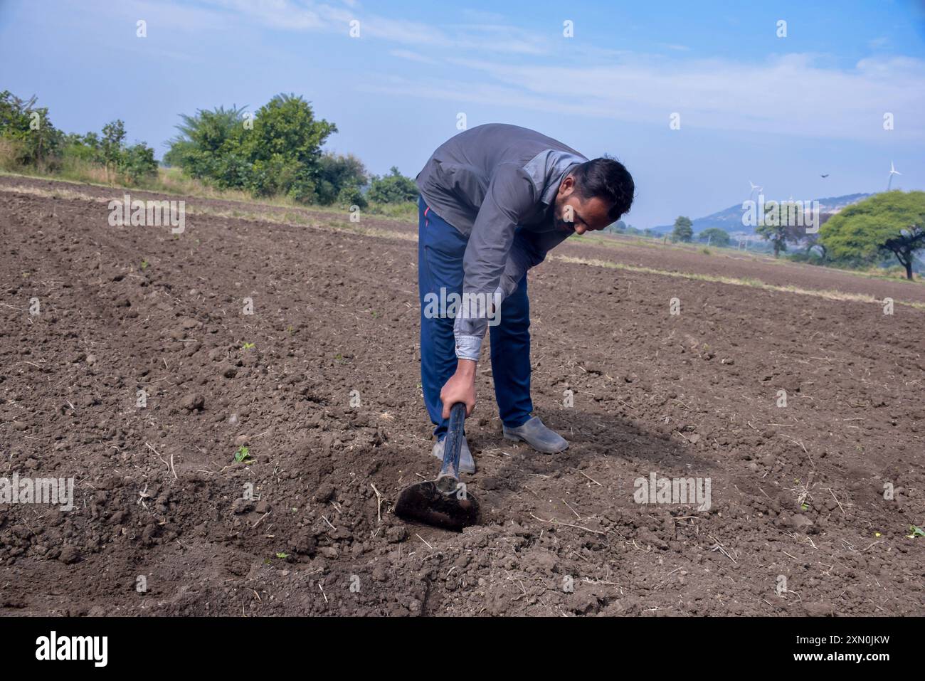 Indian farmer digging his field with a spade, farm and sky background ...