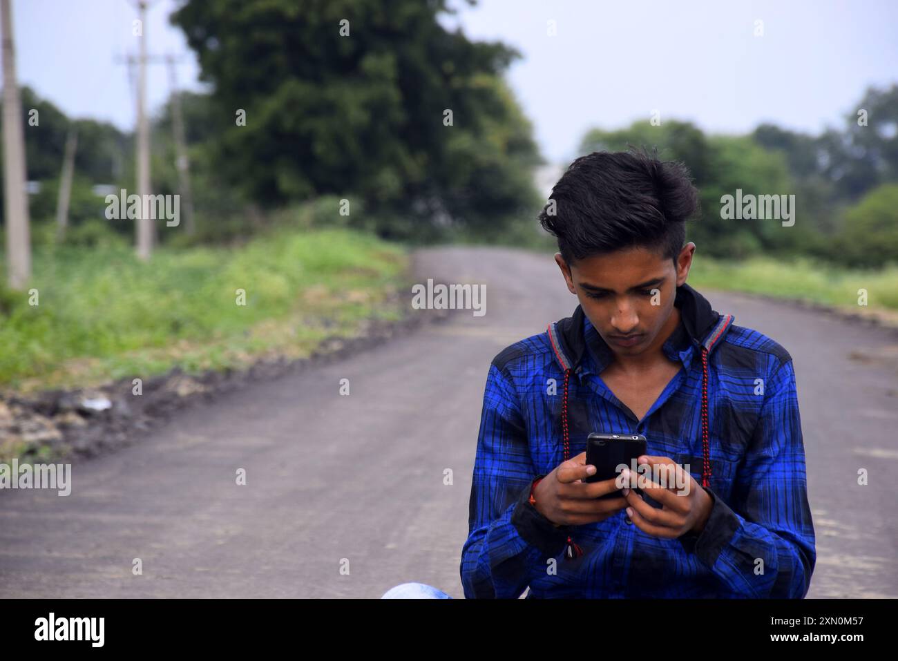 Indian teenage boy is on the street using mobile phone, in blue dress ...