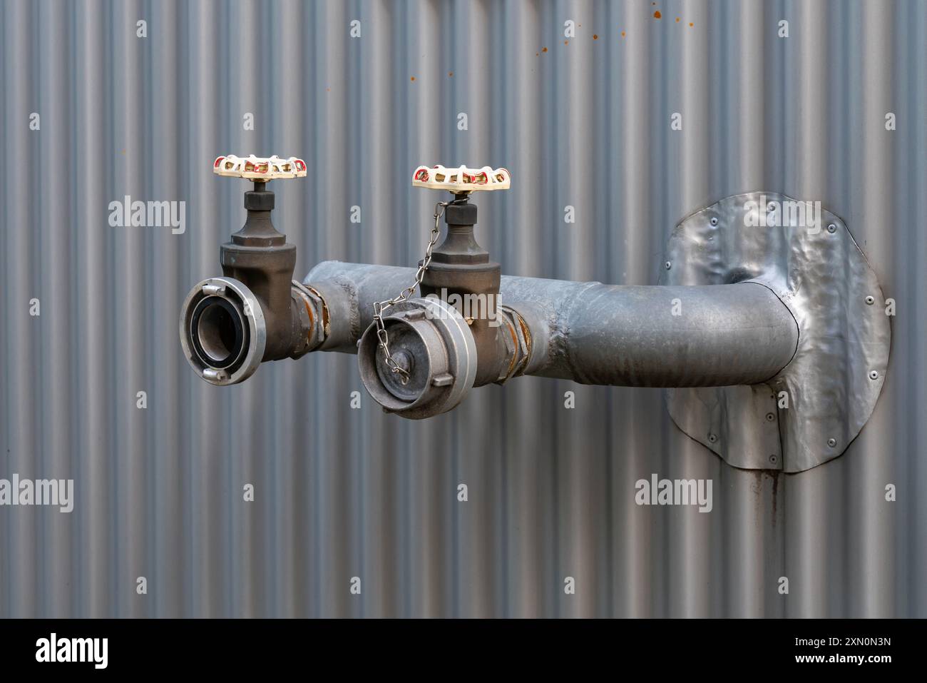 Two metal valves are mounted on a pipe structure against a gray ...