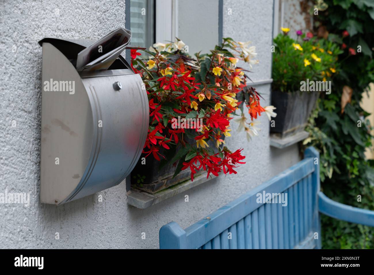 A metal mailbox with newspaper and vibrant flowers in a window box on ...
