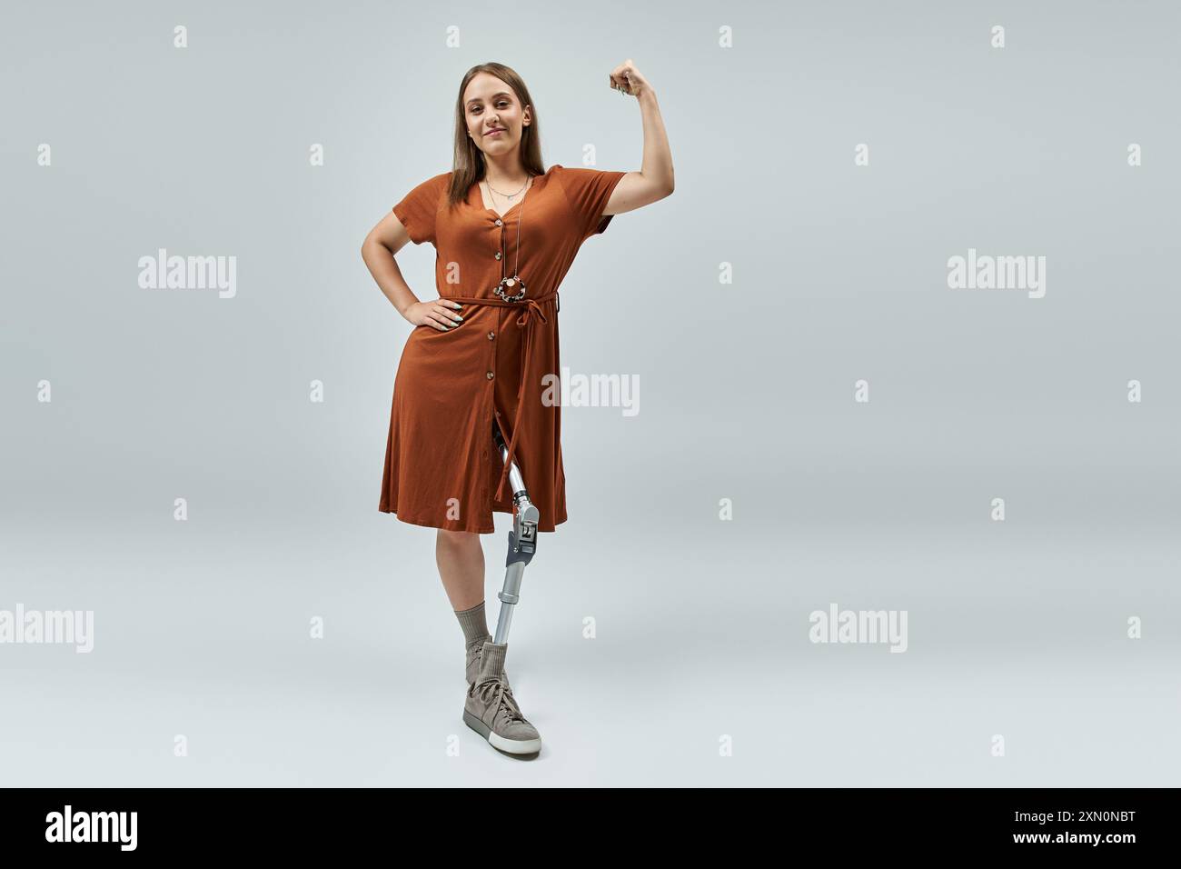 A woman in a brown dress stands with her right arm raised, showing off ...