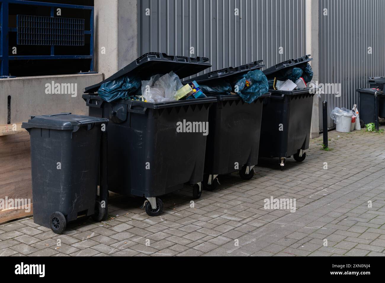 Several overflowing trash bins filled with waste are lined up outside a ...