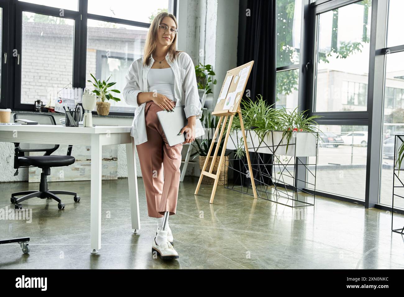 A woman with a prosthetic leg leans on a desk in an office space ...